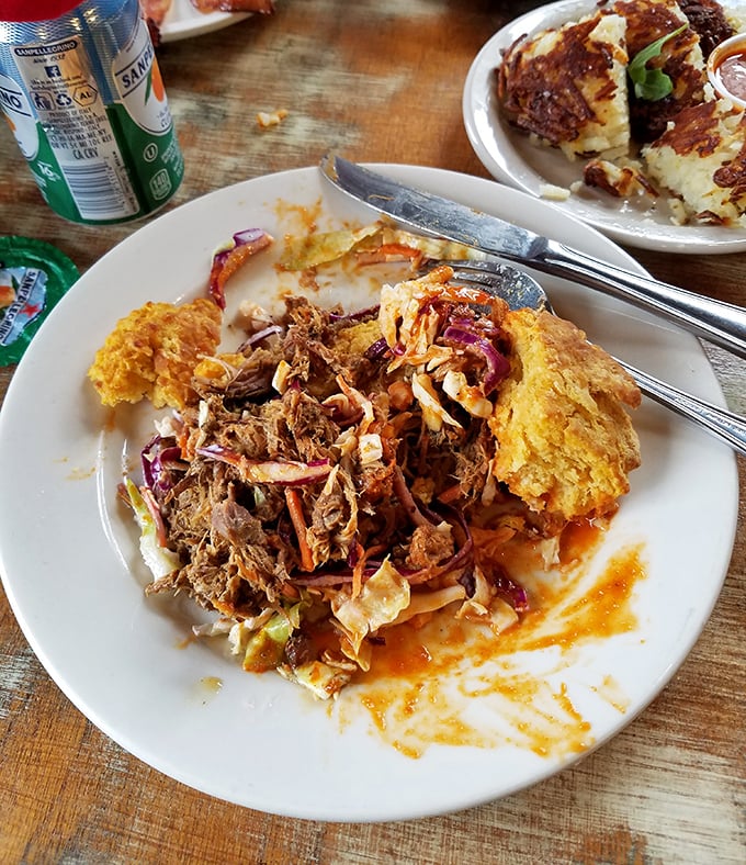 Pulled pork nestled between orange-tinted biscuit halves creates a symphony of textures. The sauce dripping down the sides isn't messy—it's a promise.