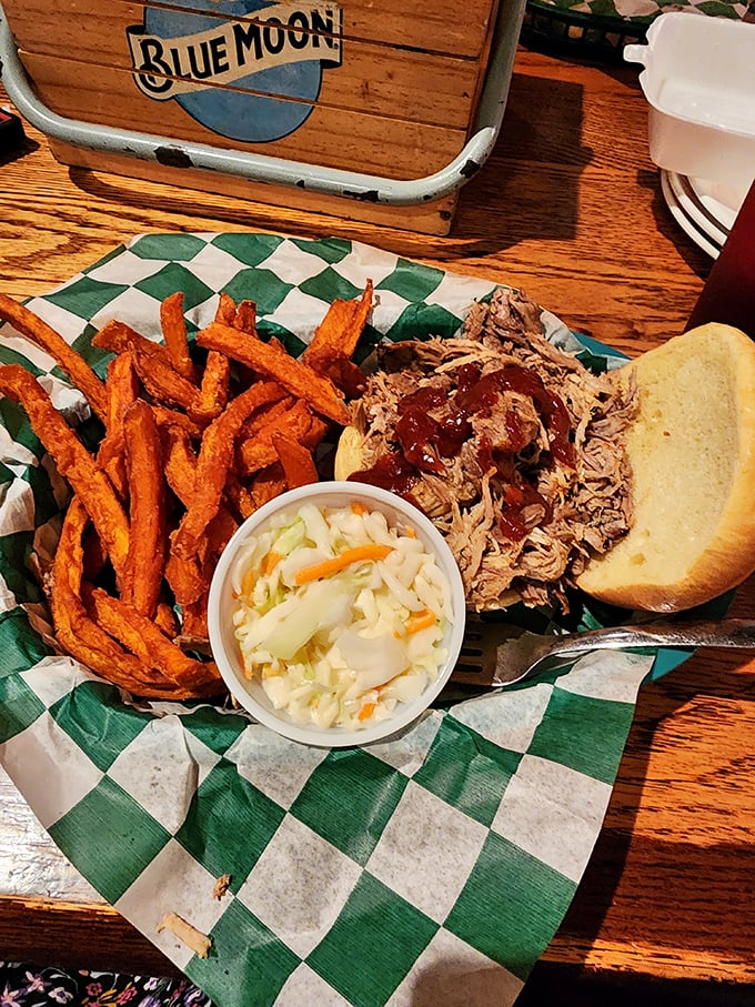 Sweet potato fries, tangy slaw, and pulled pork on a checkered paper – the holy trinity of BBQ satisfaction. Blue Moon in the background suggests divine pairing.