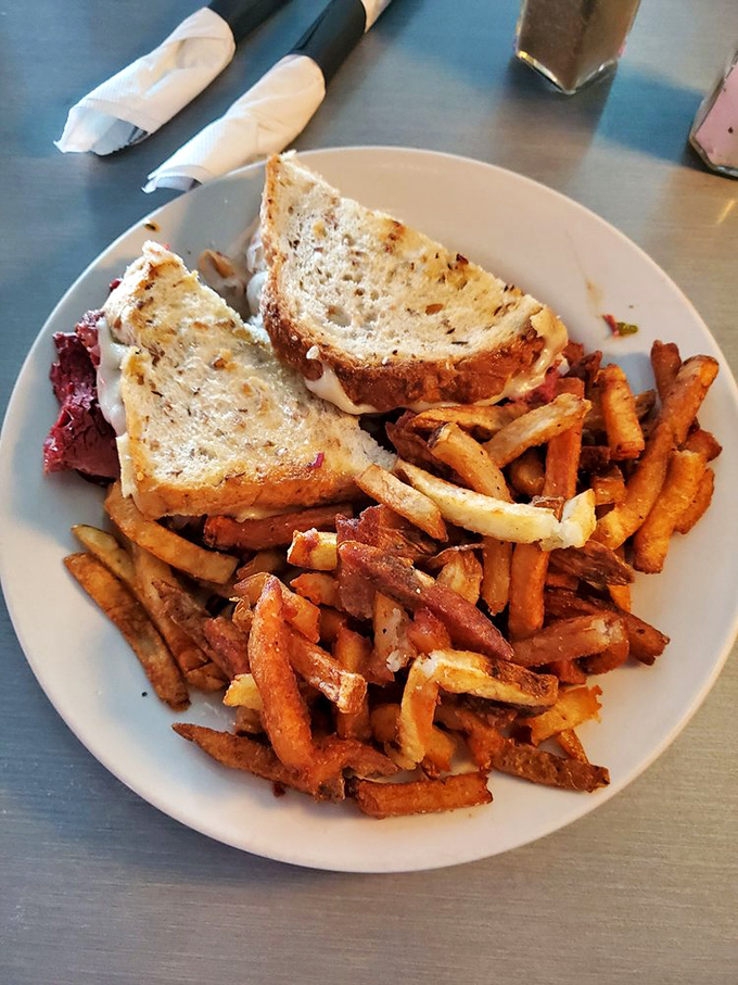 A sandwich with architectural integrity. Grilled bread barely contains what appears to be a classic Reuben, while those fries deserve their own zip code.