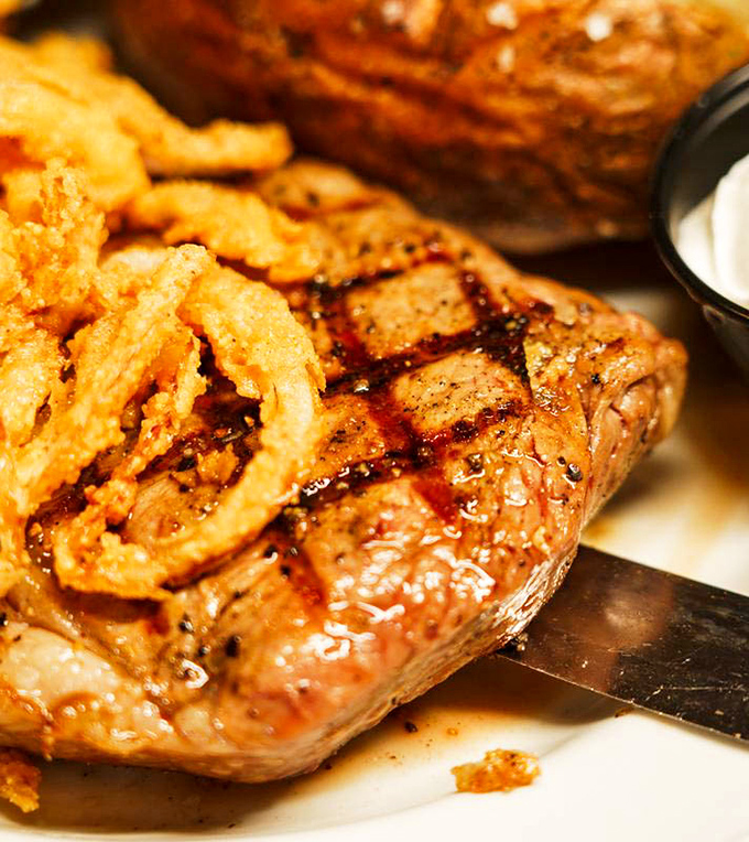 This ribeye doesn't just sit on the plate—it commands attention with perfect grill marks and a crown of crispy onions.