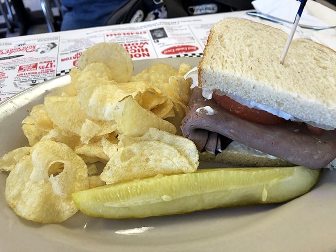 A sandwich so straightforward it doesn't need to brag—white bread, cold cuts, chips, and a pickle spear that stands at attention.