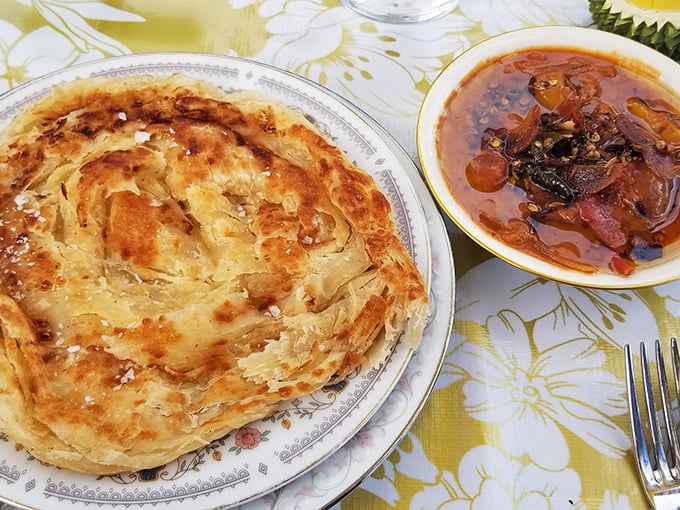 The holy grail of flatbreads—roti canai with its hypnotic spiral of flaky layers that shatter with each heavenly tear.