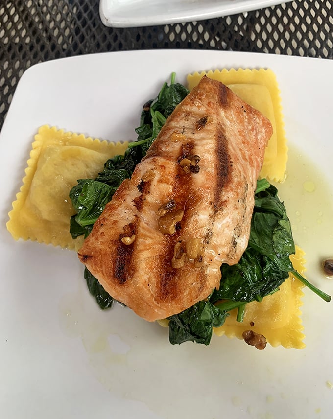 Perfectly seared salmon resting on a bed of spinach and ravioli – proof that tavern food can dance gracefully between rustic and refined.