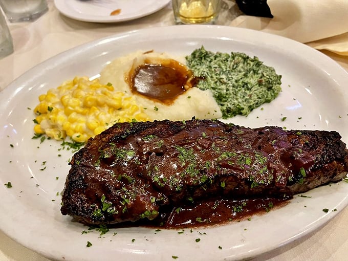 A New York steak glistening with savory goodness, flanked by creamed corn, spinach, and mashed potatoes. The holy trinity of steakhouse sides.