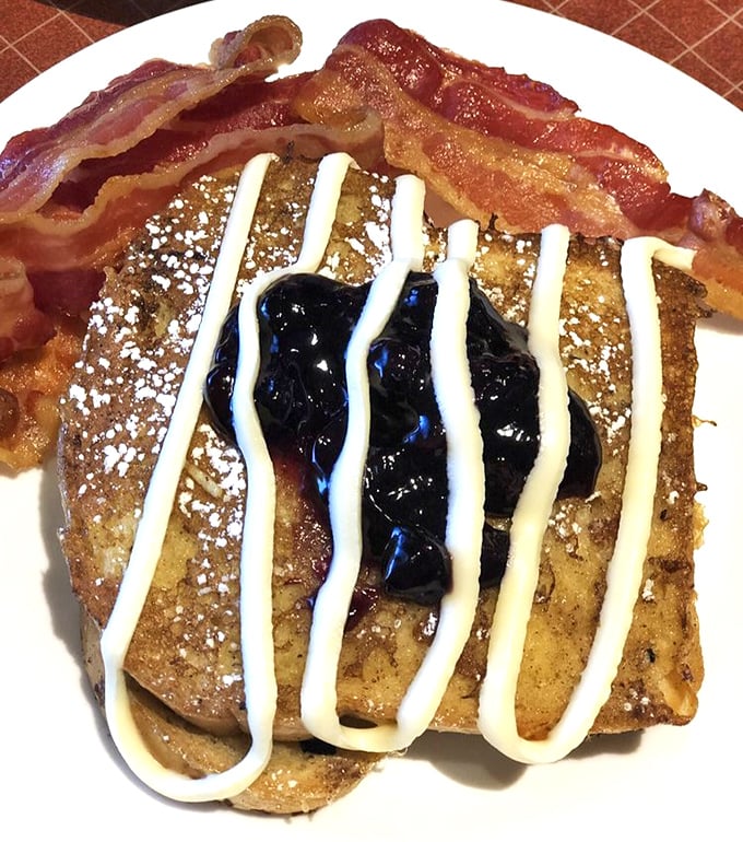 French toast that's having an identity crisis as dessert, complete with berry compote, cream drizzle, and bacon standing guard. Breakfast perfection!