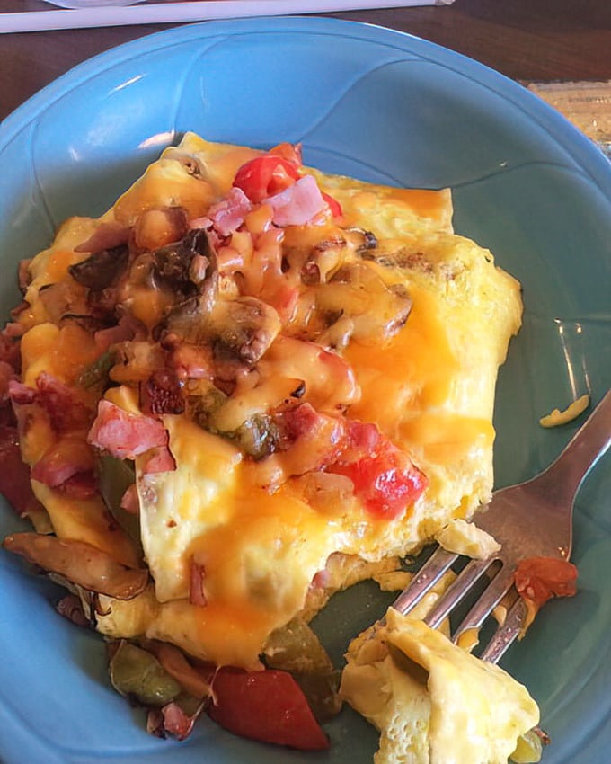The supreme omelet arrives like a sunrise on a plate—cheese cascading over farm-fresh eggs studded with vegetables and ham.