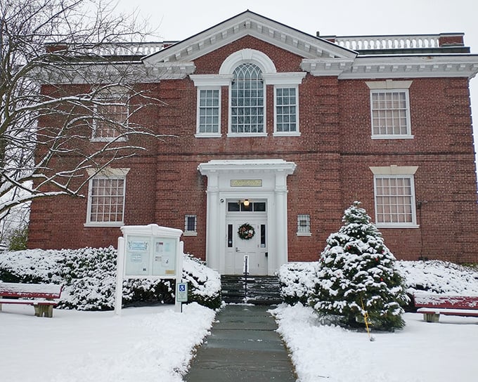 Snow dusts this stately brick building like powdered sugar, creating a perfect winter postcard moment.