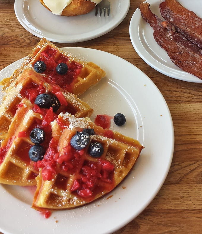 These waffles aren't just topped with berries – they're wearing them like jewelry. That bacon on the side is just showing off.