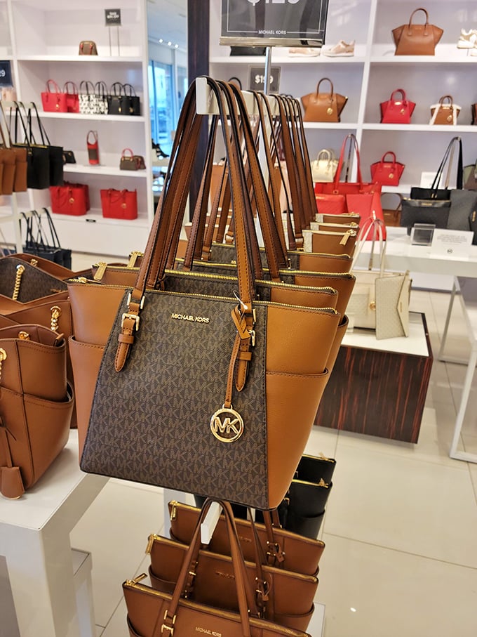 The handbag display at Michael Kors – where leather dreams come with gold hardware and the promise of organized chaos inside.
