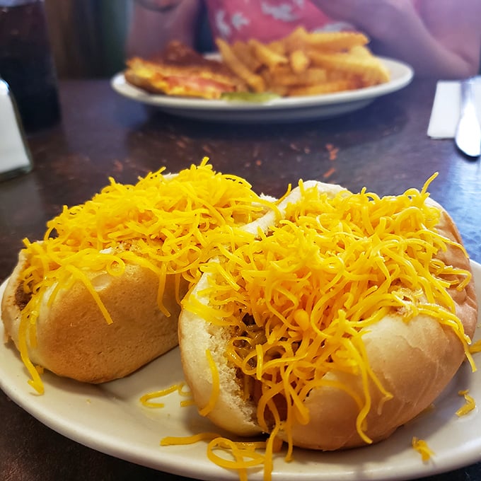 Behold the cheese coney in its natural habitat—a mountain of finely shredded cheddar creating a protective orange blanket over Cincinnati's signature contribution to hot dog artistry.
