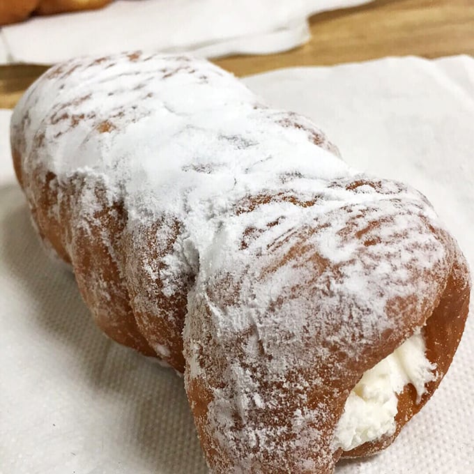 The cream horn – where powdered sugar meets cloud-like filling in a delicate pastry embrace. Worth every napkin you'll need afterward.