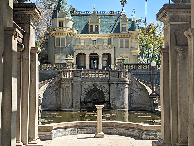 The mansion's façade, viewed through classical columns, looks like it's posing for its architectural glamour shot. Downton Abbey, California-style.