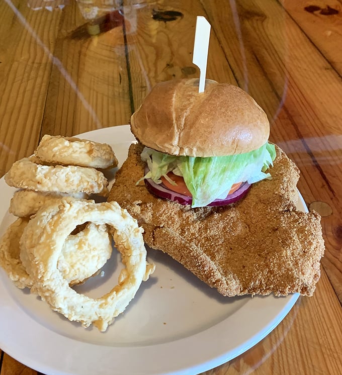 This isn't just a sandwich, it's architectural achievement – crispy breaded tenderloin, fresh toppings, and those onion rings deserve their own zip code.