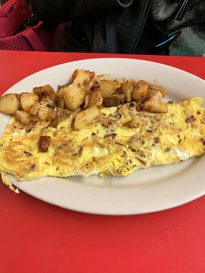 Breakfast perfection on a plate – a golden omelet nestled beside those famous home fries, the kind of honest cooking that makes morning people out of night owls.