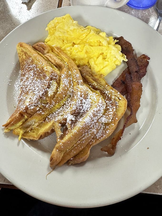 French toast dusted with powdered sugar, scrambled eggs, and bacon—the breakfast trinity that makes getting out of bed before noon entirely worthwhile.