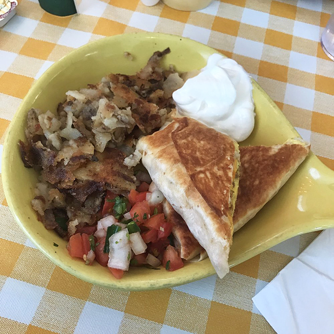A hearty breakfast served on a sunny yellow plate – home fries, fresh pico, and a quesadilla that means business.