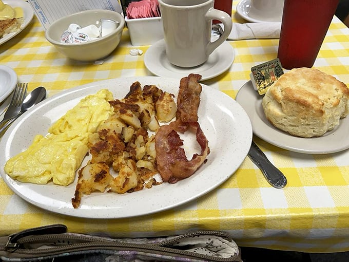 The breakfast trinity – fluffy scrambled eggs, golden hash browns, and bacon cooked to that perfect point between chewy and crisp, with a biscuit standing by.
