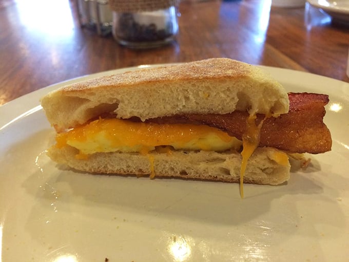 The breakfast sandwich in its natural habitat—melty cheese escaping the edges like it's making a delicious jailbreak. Worth setting your alarm for.