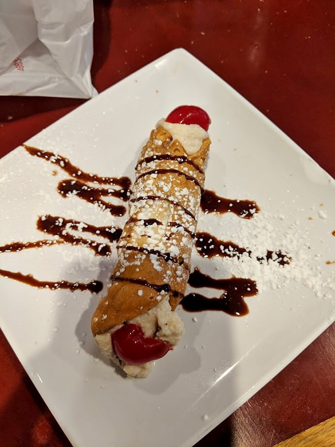 Not just any cannoli—this crisp shell filled with sweet cream, adorned with chocolate drizzle and cherries, is dessert architecture at its finest.