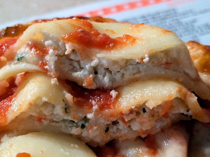 The cheese ravioli cross-section reveals the truth—pillowy pasta pockets filled with herb-flecked ricotta, all swimming in that signature sauce that haunts your dreams.
