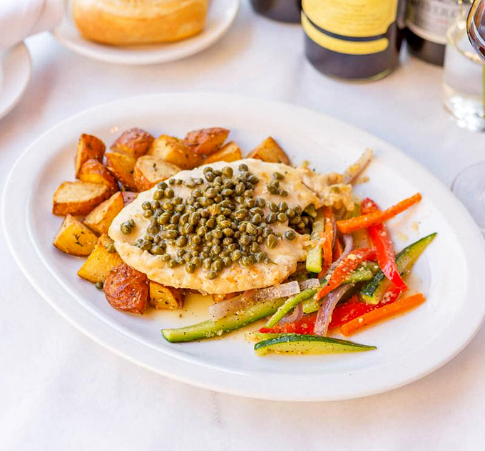 The Chicken Piccata speaks the universal language of comfort—golden cutlets crowned with briny capers alongside colorful vegetables and roasted potatoes.