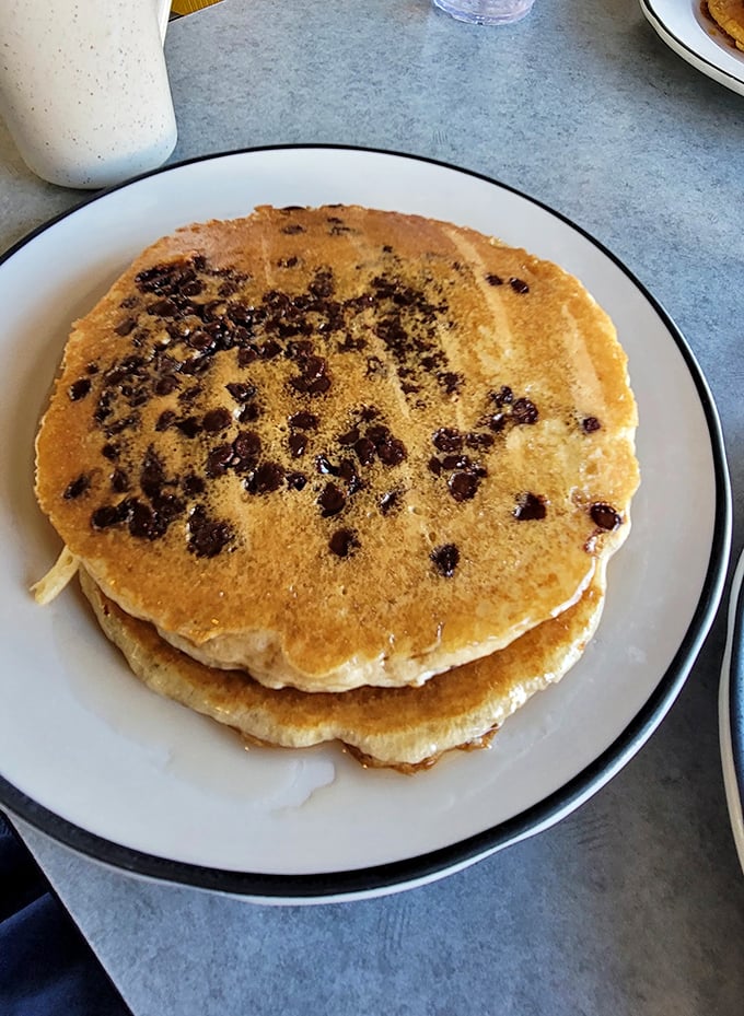 Chocolate chip pancakes that would make Willy Wonka jealous—golden discs studded with melty chocolate morsels waiting for their maple bath.