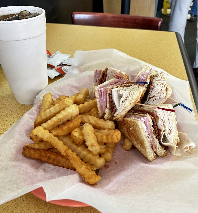 The club sandwich—that multi-story skyscraper of deli engineering—paired with crinkle-cut fries that audibly crunch with each bite.