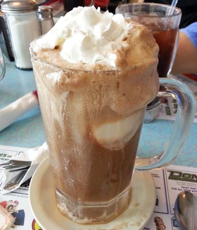 This isn't just a coffee-colored soda—it's a frothy time capsule of soda fountain culture, topped with a cloud of whipped cream that defies gravity.