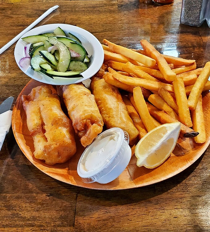 Fish and chips served on a wooden plate with cucumber salad – proof that simplicity, when done right, is the ultimate sophistication.