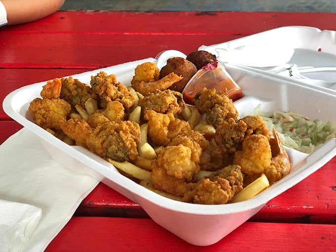 Fried clams and fries served in a simple foam container on a red picnic table. No white tablecloth needed when the seafood is this fresh.