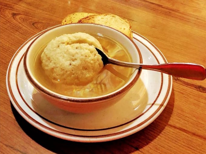 The matzo ball soup—featuring a dumpling so perfectly formed it deserves its own zip code, floating majestically in golden broth that tastes like liquid comfort.