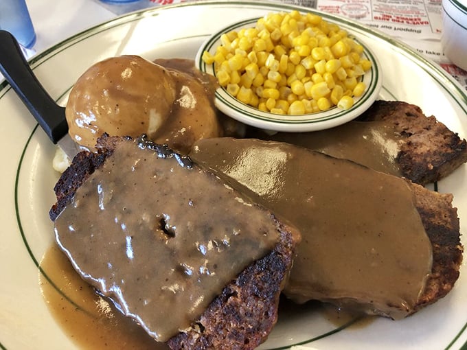 Meatloaf swimming in gravy with a side of sweet corn—the kind of plate that makes you want to call your mother and apologize.