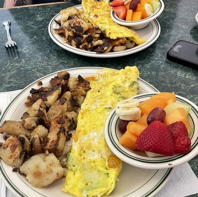 Two plates showcasing the art of the perfect omelet – folded like a letter containing good news, alongside home fries that deserve their own fan club.