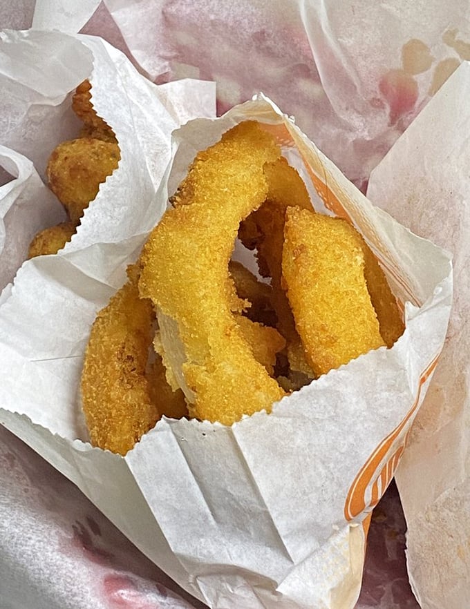 Golden-fried onion rings nestled in paper like precious artifacts. These crispy halos aren't just side dishes—they're the main event masquerading as supporting characters.