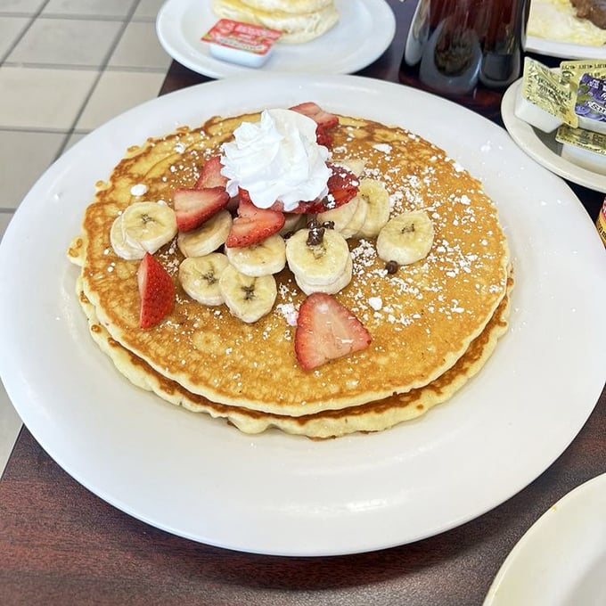 Golden pancakes adorned with fresh fruit and a dusting of powdered sugar—proof that sometimes the classics need no improvement, just quality execution.
