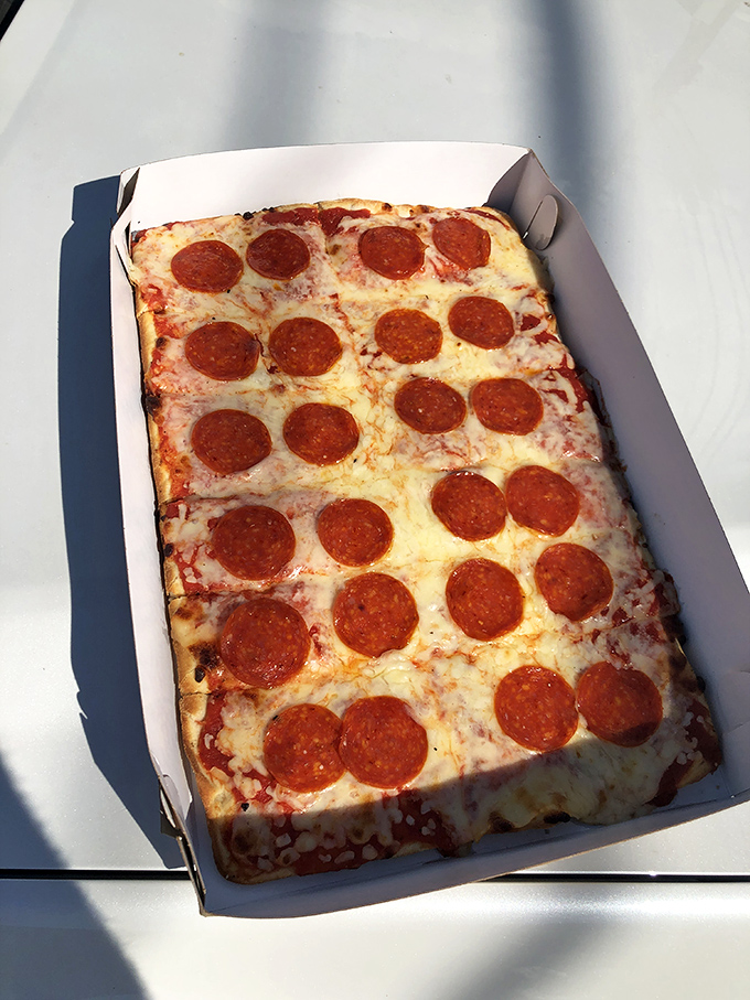 The rectangular pepperoni pizza—or "tray" in local parlance—showcases perfectly spaced pepperoni discs that curl up at the edges, creating tiny cups of savory goodness.