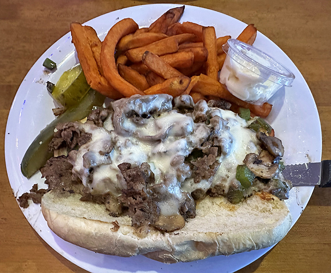 Behold the Philly cheesesteak in its natural habitat—smothered in mushrooms and melty cheese. The sweet potato fries alongside are no mere sidekick.