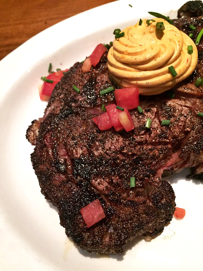 This blackened ribeye wears its char like a badge of honor. Topped with compound butter and diced tomatoes, it's a carnivore's dream come true.