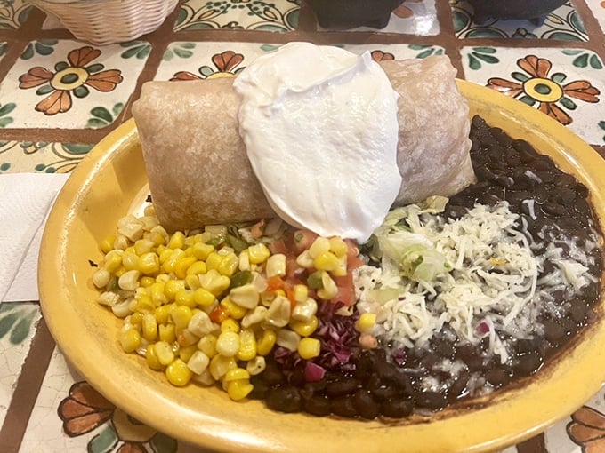 A burrito that demands respect, flanked by black beans studded with corn and a colorful pico de gallo that brightens the entire plate.