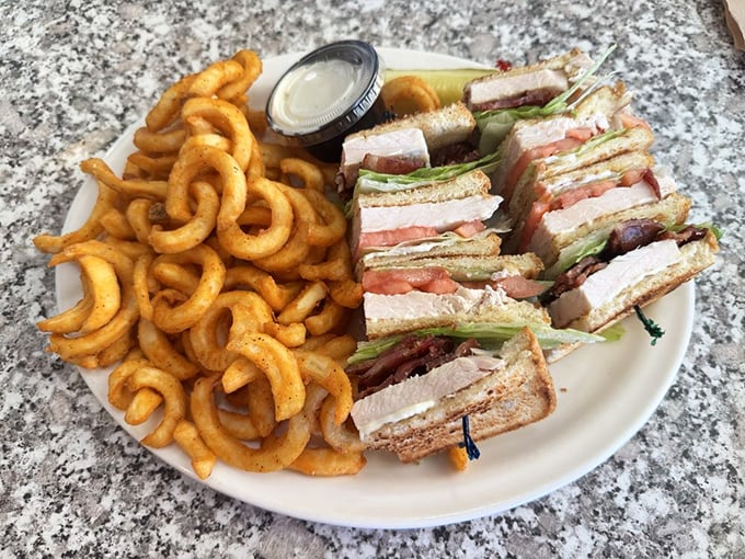The legendary club sandwich arrives with curly fries—architectural perfection between bread slices that would make Frank Lloyd Wright jealous.