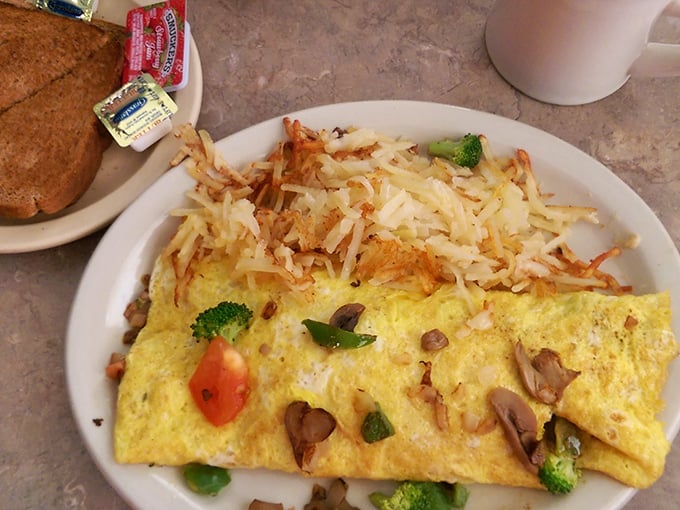 Breakfast artistry at its finest—a fluffy omelet stuffed with fresh vegetables and crowned with a snowfall of hash browns that puts ordinary morning meals to shame.