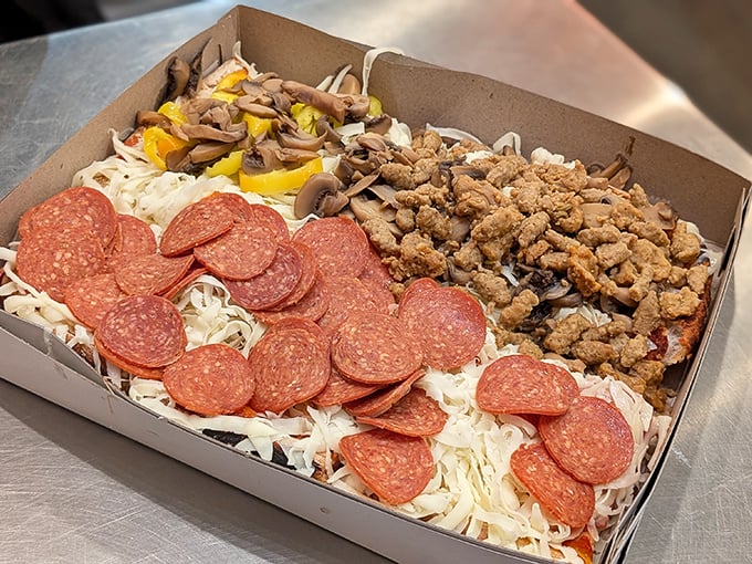Pizza artistry in its final form – pepperoni, sausage, and mushrooms creating a topping trifecta atop that signature bed of unmelted cheese.