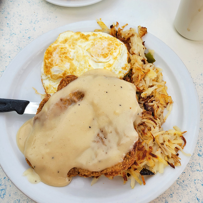 Country fried steak smothered in gravy alongside crispy hash browns and sunny-side-up eggs—the breakfast equivalent of a warm hug from your favorite aunt.