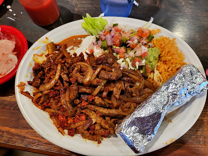 The fajita platter arrives with that signature sizzle—a symphony of perfectly grilled meat alongside colorful accompaniments and a foil-wrapped burrito sidekick.