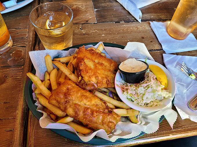 The fish and chips arrive like golden treasures on a wooden plank—crispy batter protecting flaky white fish beside perfectly cooked fries.