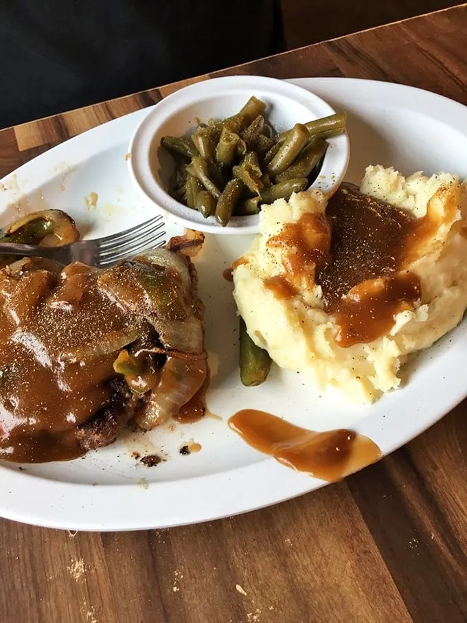 A plate that tells the whole Midwest story—tender meat smothered in rich gravy, mashed potatoes with just enough lumps to prove they're real, and green beans that haven't forgotten their vegetable heritage.