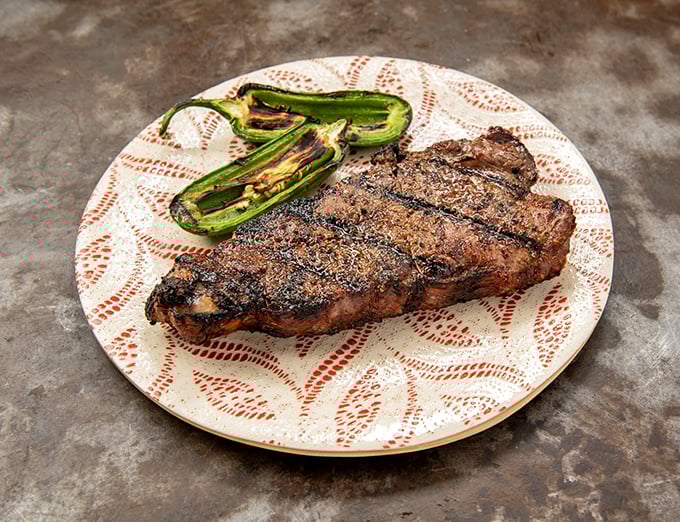 A steak and grilled jalapeños on a decorative plate – proof that in Texas, even fancy dishware knows its supporting role.