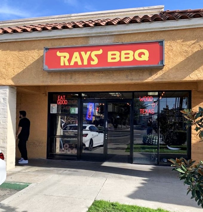 Ray's vibrant storefront with its neon "OPEN" sign is like a beacon for lost souls seeking authentic Texas smoke in Southern California.