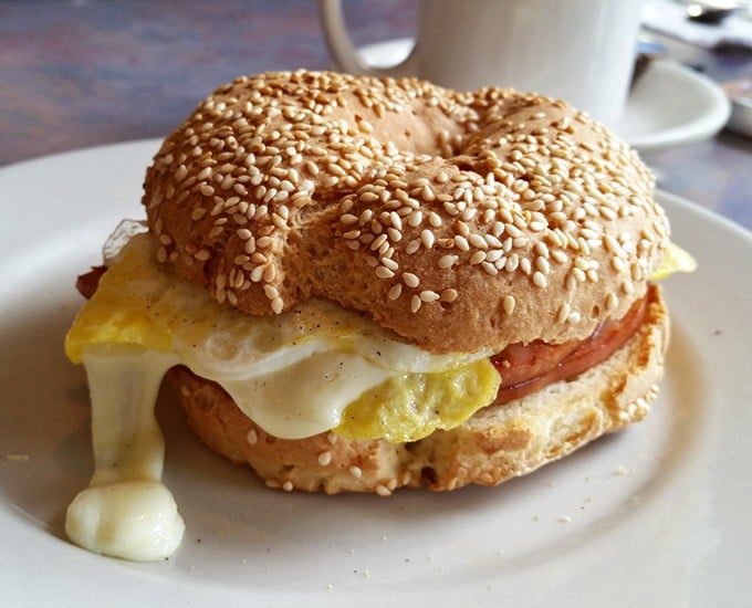 Breakfast sandwich architecture at its finest – the sesame bagel foundation supporting that glorious egg-cheese-meat trifecta.