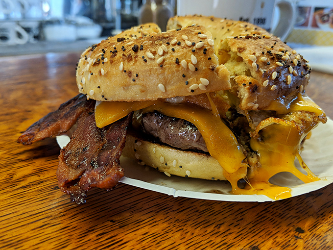 This isn't just a bagel burger—it's architecture. The melted cheese forms structural support for bacon that defies gravity and good sense.